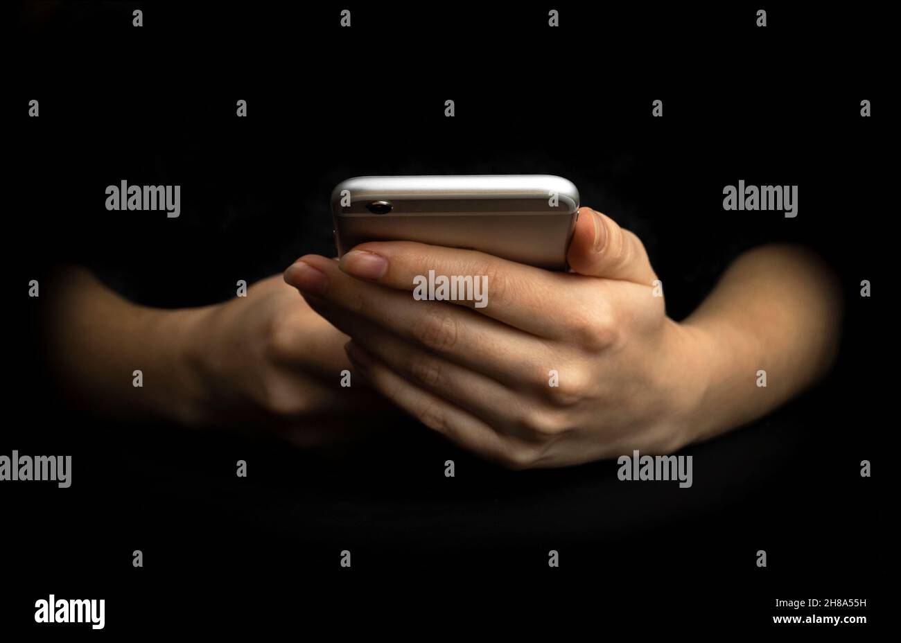 Person uses mobile phone, front view. Black background, hands and ...