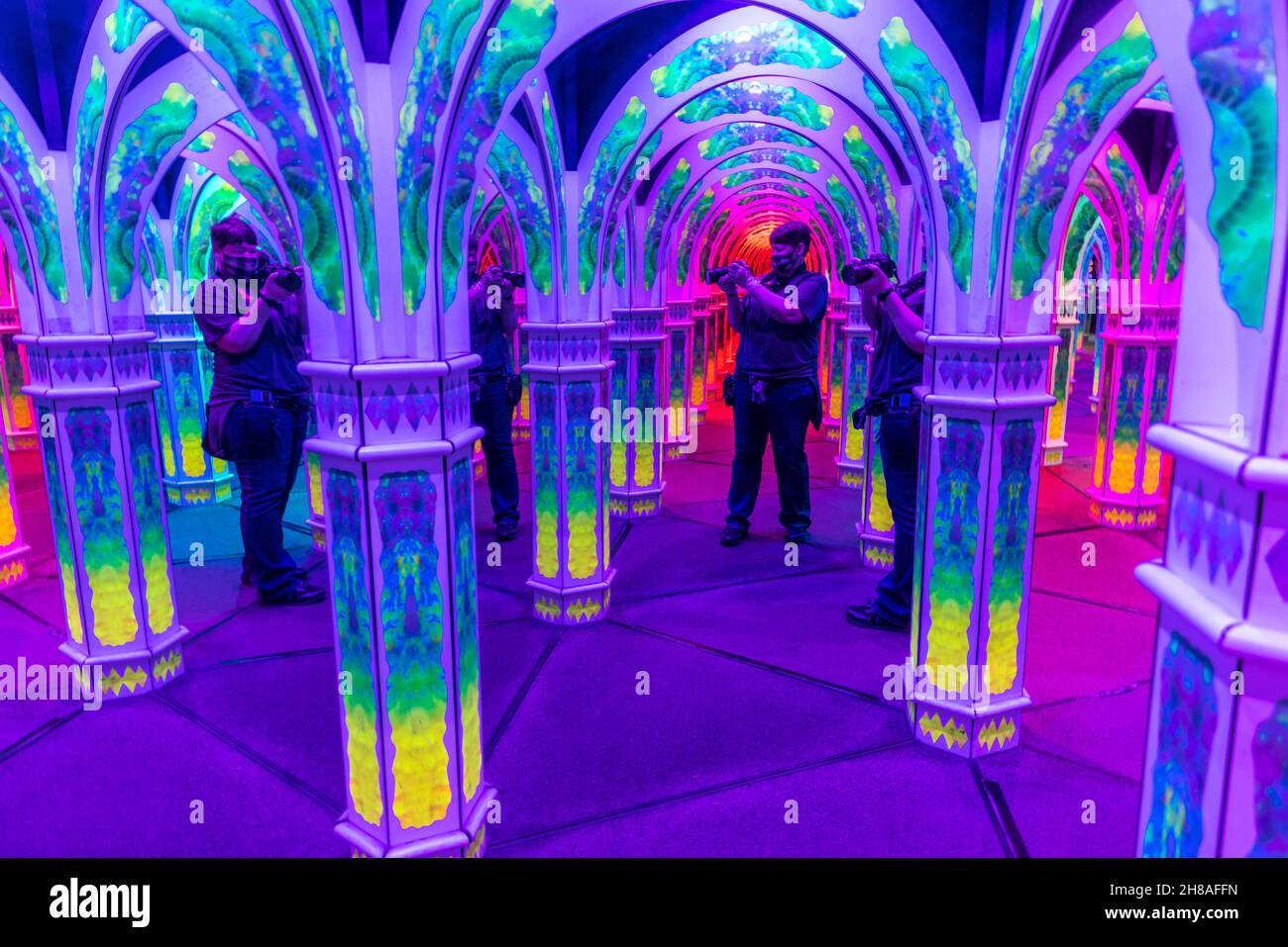 Person walking through a maze of mirrors in neon light using a camera ...