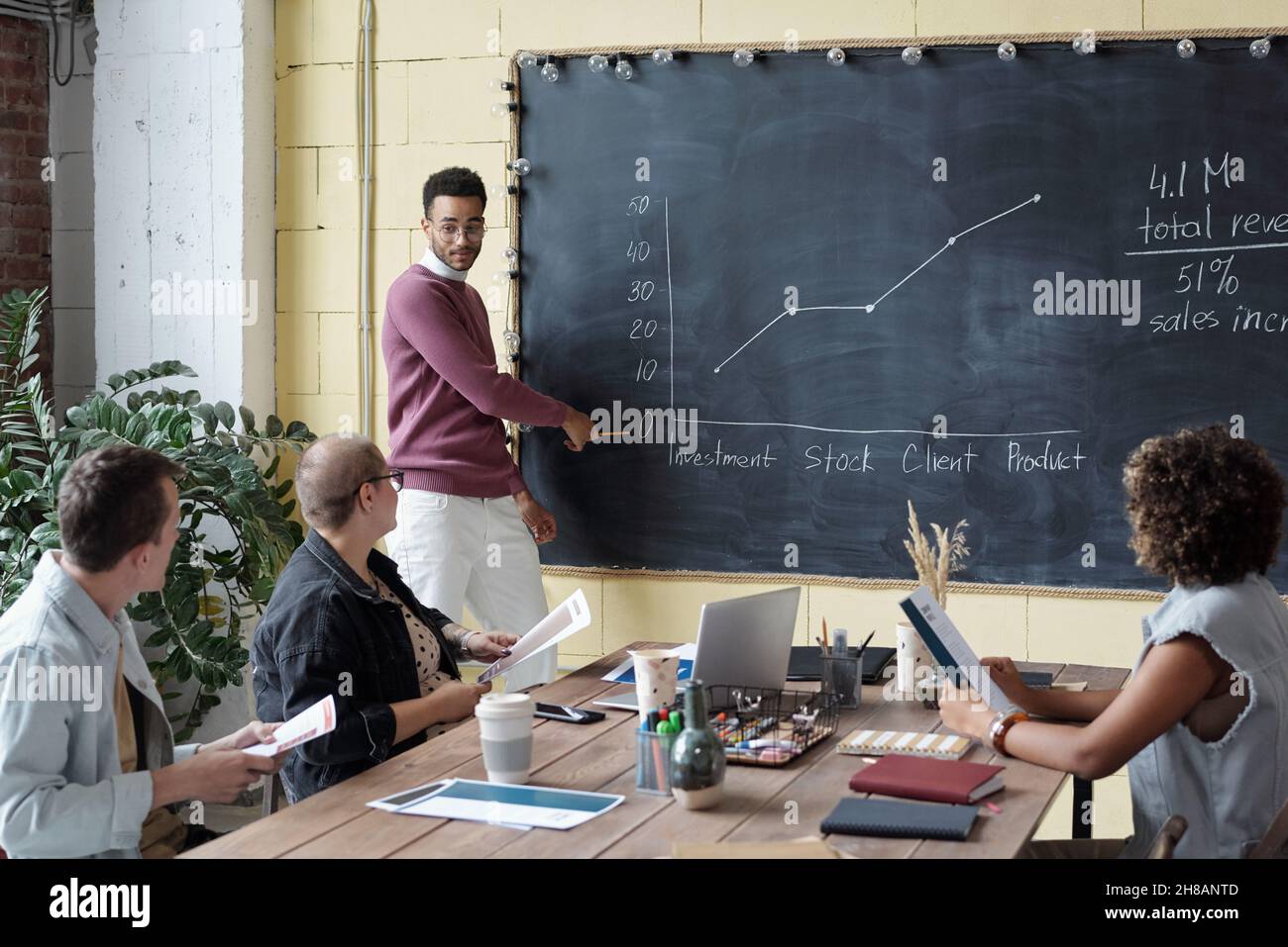 Young confident coach pointing at blackboard with graph drawn with ...