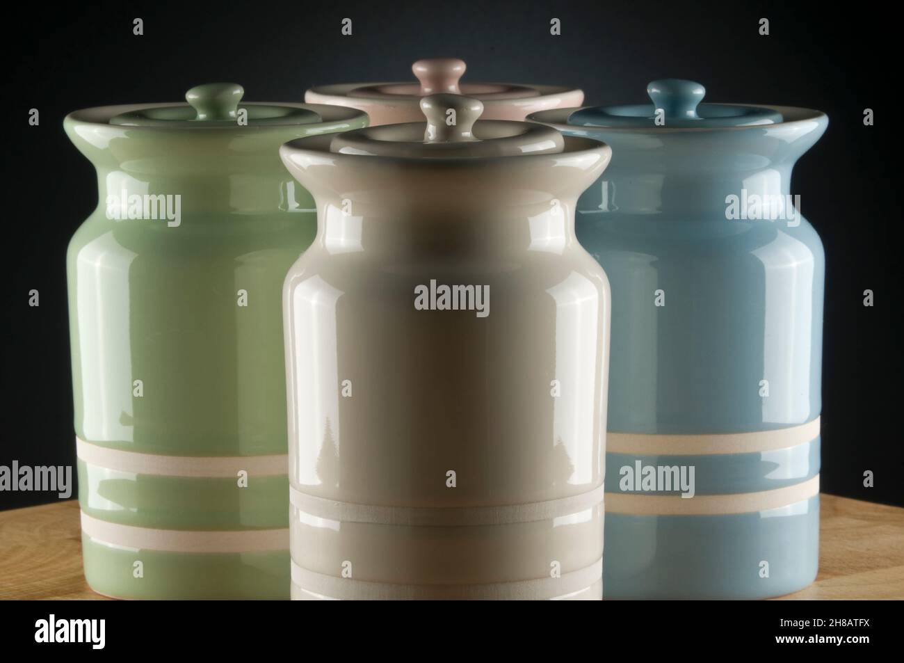 Four colourful ceramic canisters on timber bench with grey spot on ...