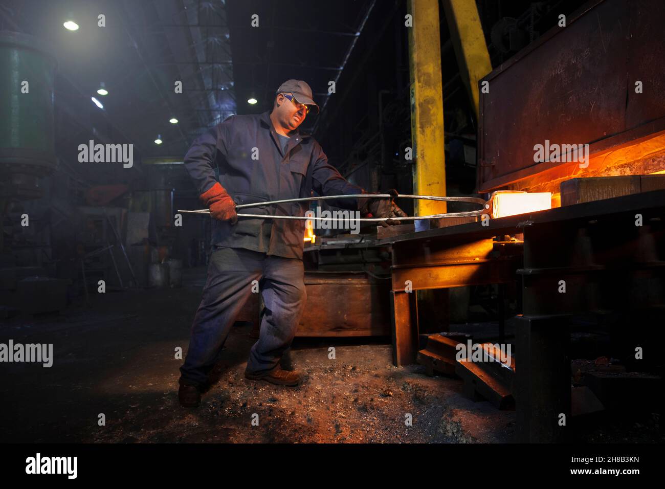Forge worker removes red hot steel billet from furnace for forging into ...