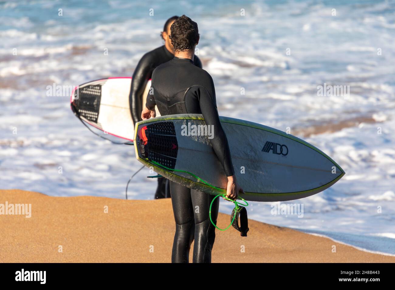 Two male adult surfers I wetsuits on the beach preparing to go surfing ...