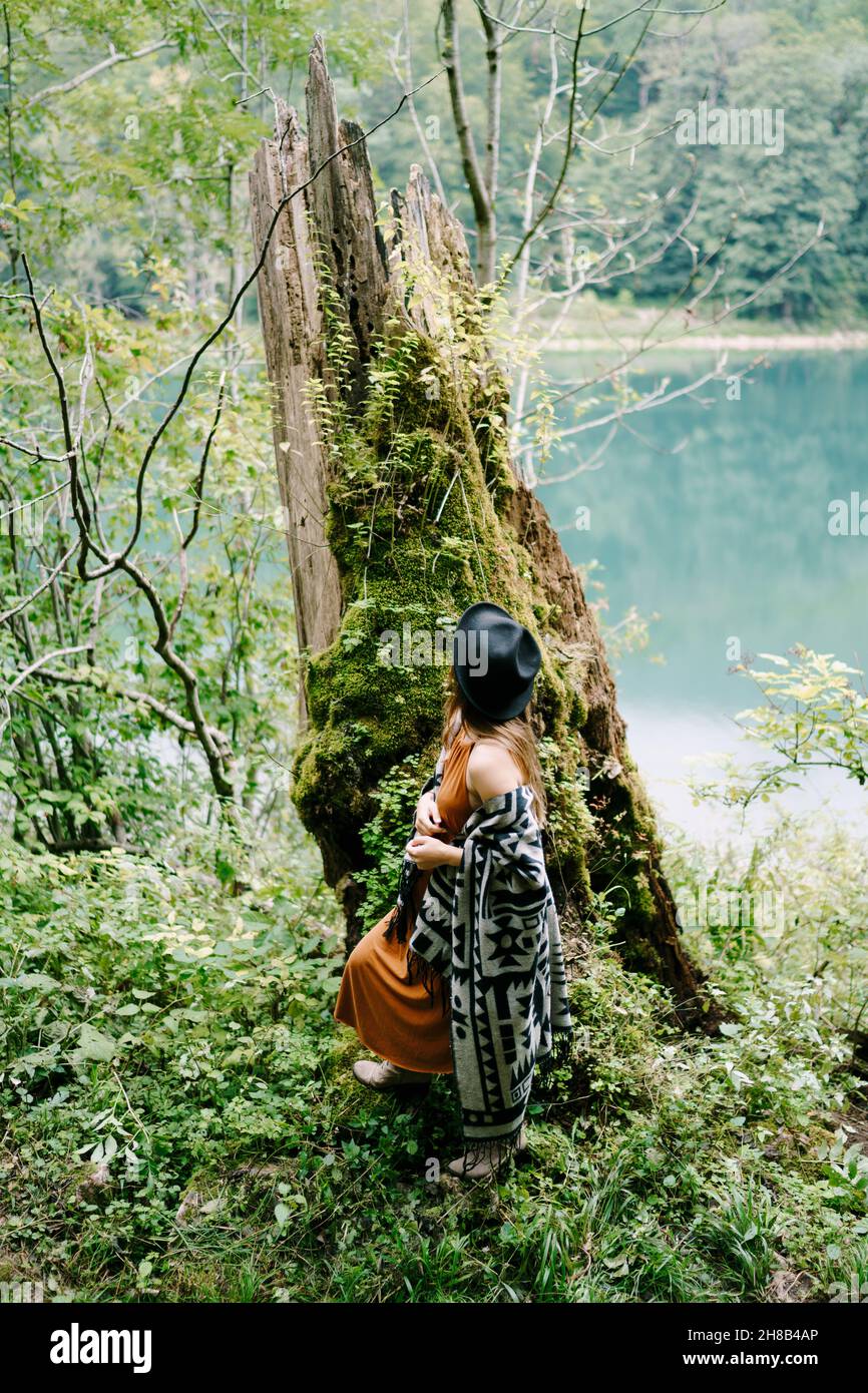 Pregnant woman stands near a tree covered with moss in the park. Back ...