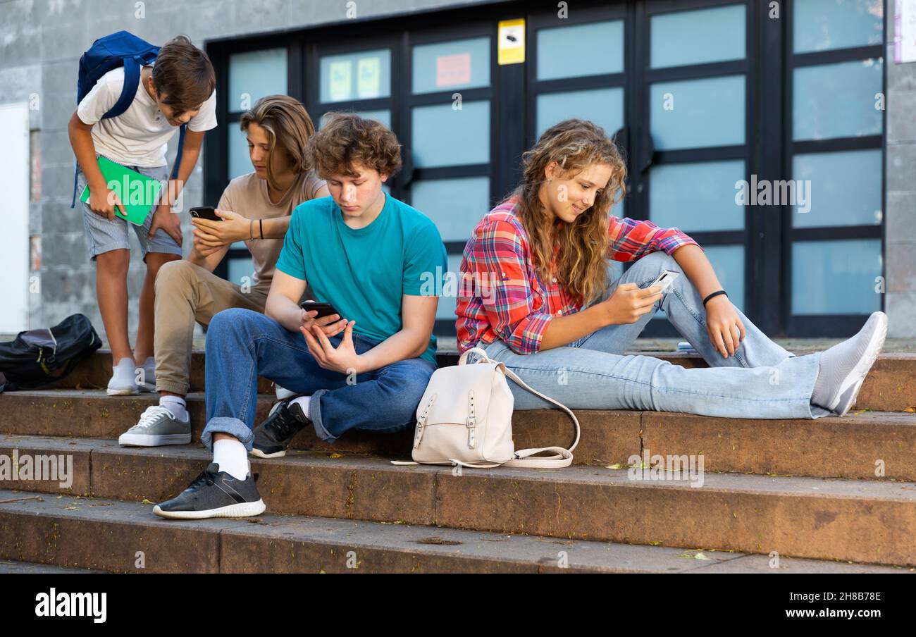 Schoolers using gadgets on break outside college Stock Photo - Alamy
