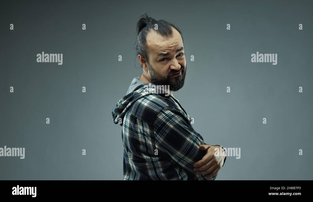 Bearded man with ponytail in csual plaid shirt looking back over his ...