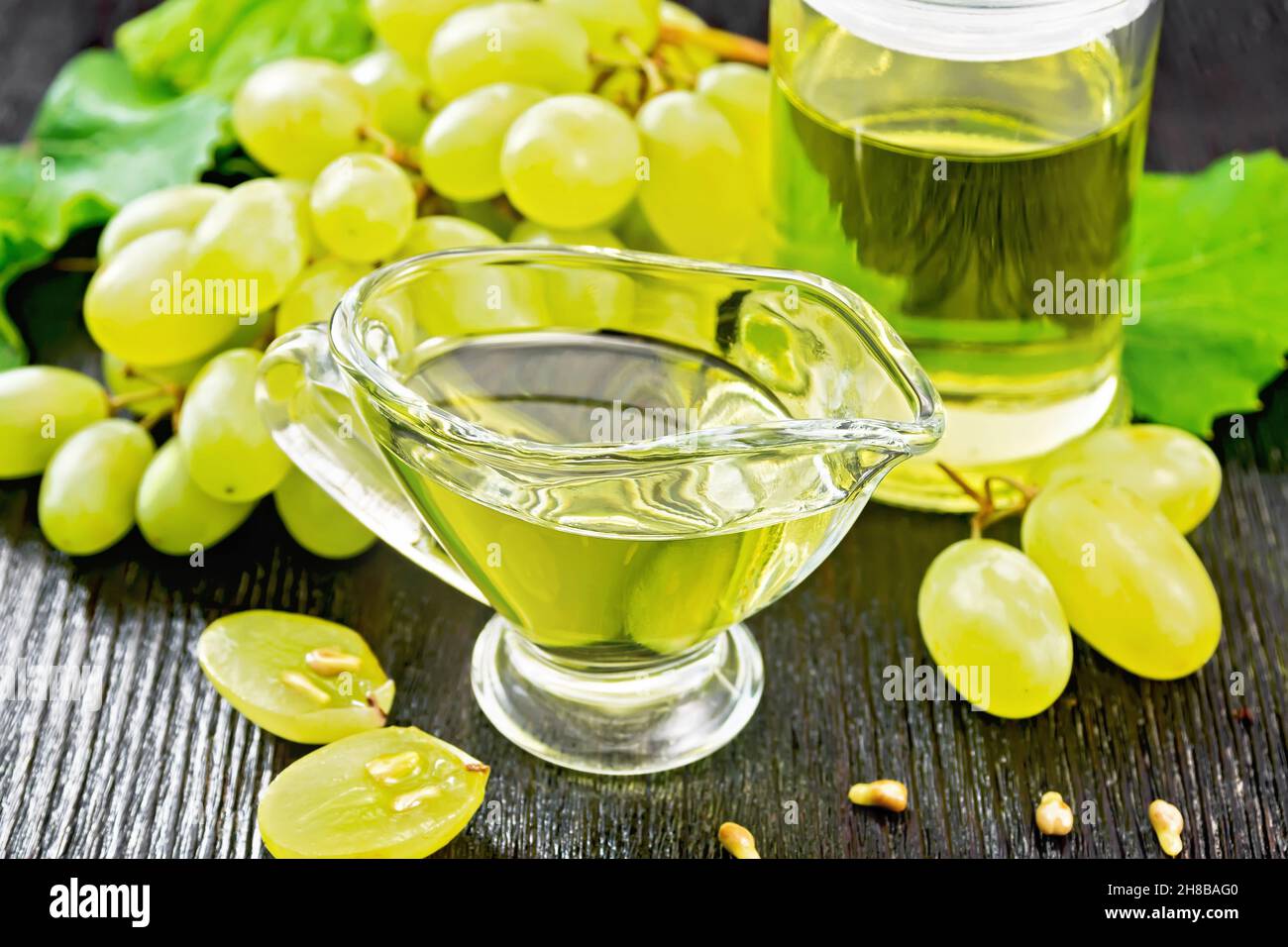 Grape oil in a gravy boat and a jar, berries of green grapes on the ...