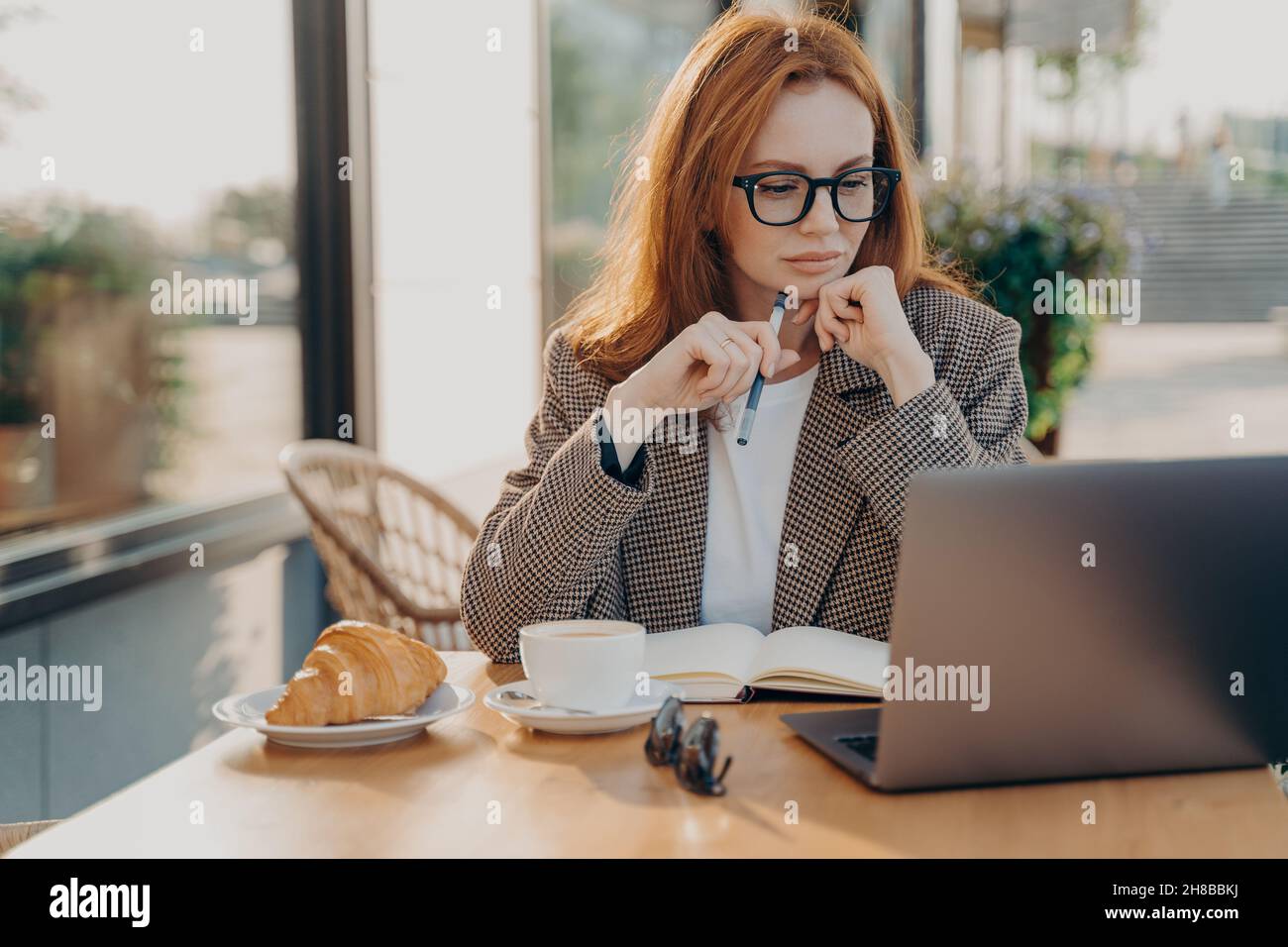 Serious ginger businesswoman in formal wear works in cafeteria develops ...