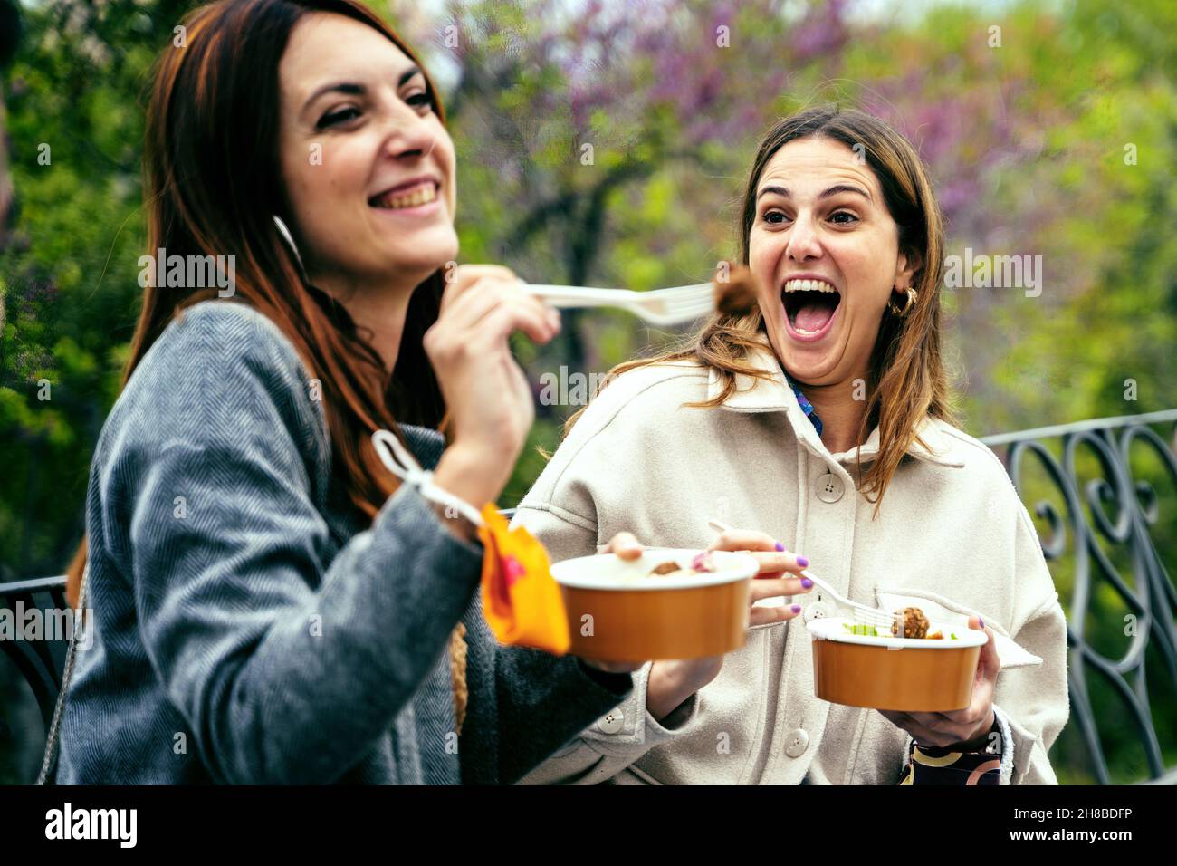 Women having fun eating take away food outdoors sitting on a bench in ...