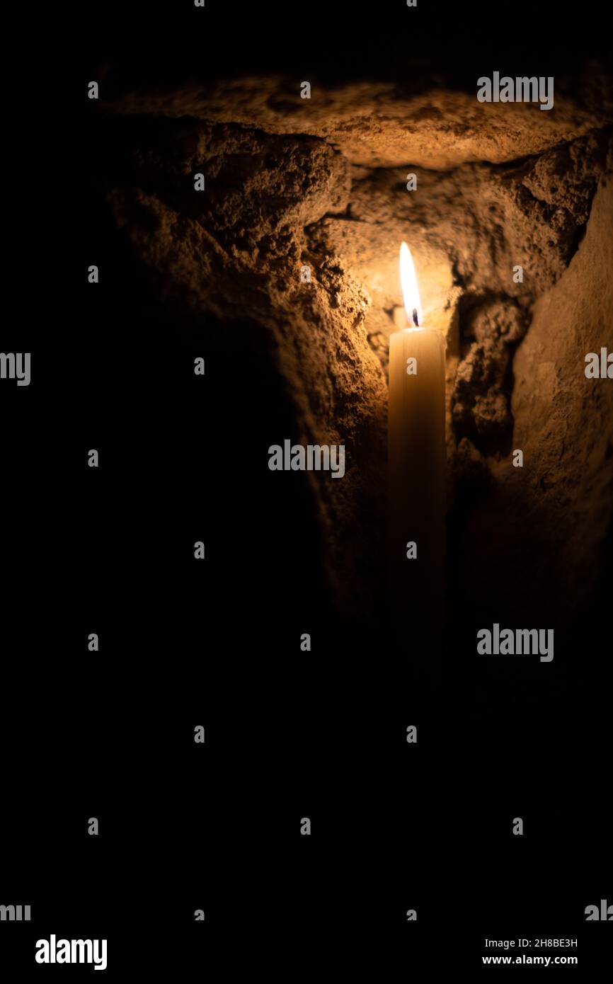 A candle burns against the background of masonry in the dark. Front ...