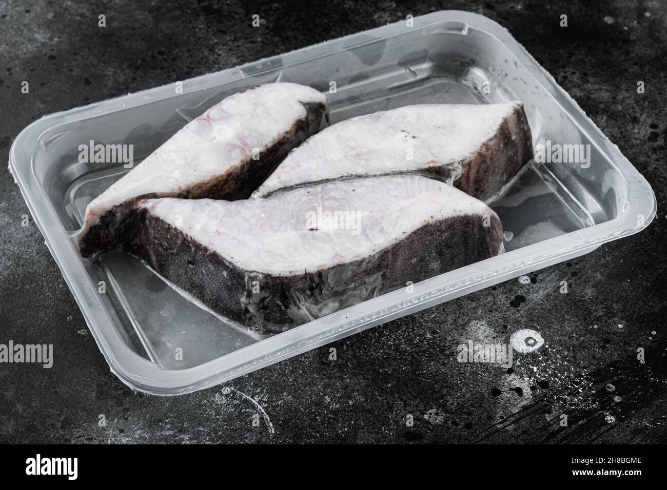 Halibut fish frozen steak pack set, on black dark stone table ...