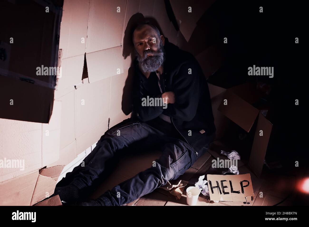 A homeless bearded man sits on boxes on street and asks for help. Need ...