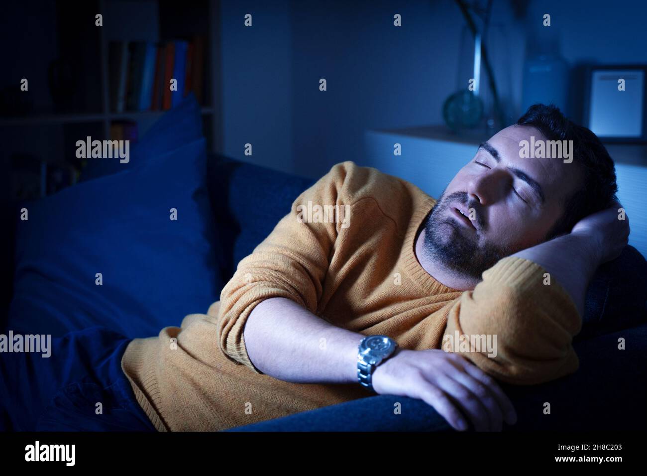 One guy sleeping on the sofa at night watching tv Stock Photo - Alamy
