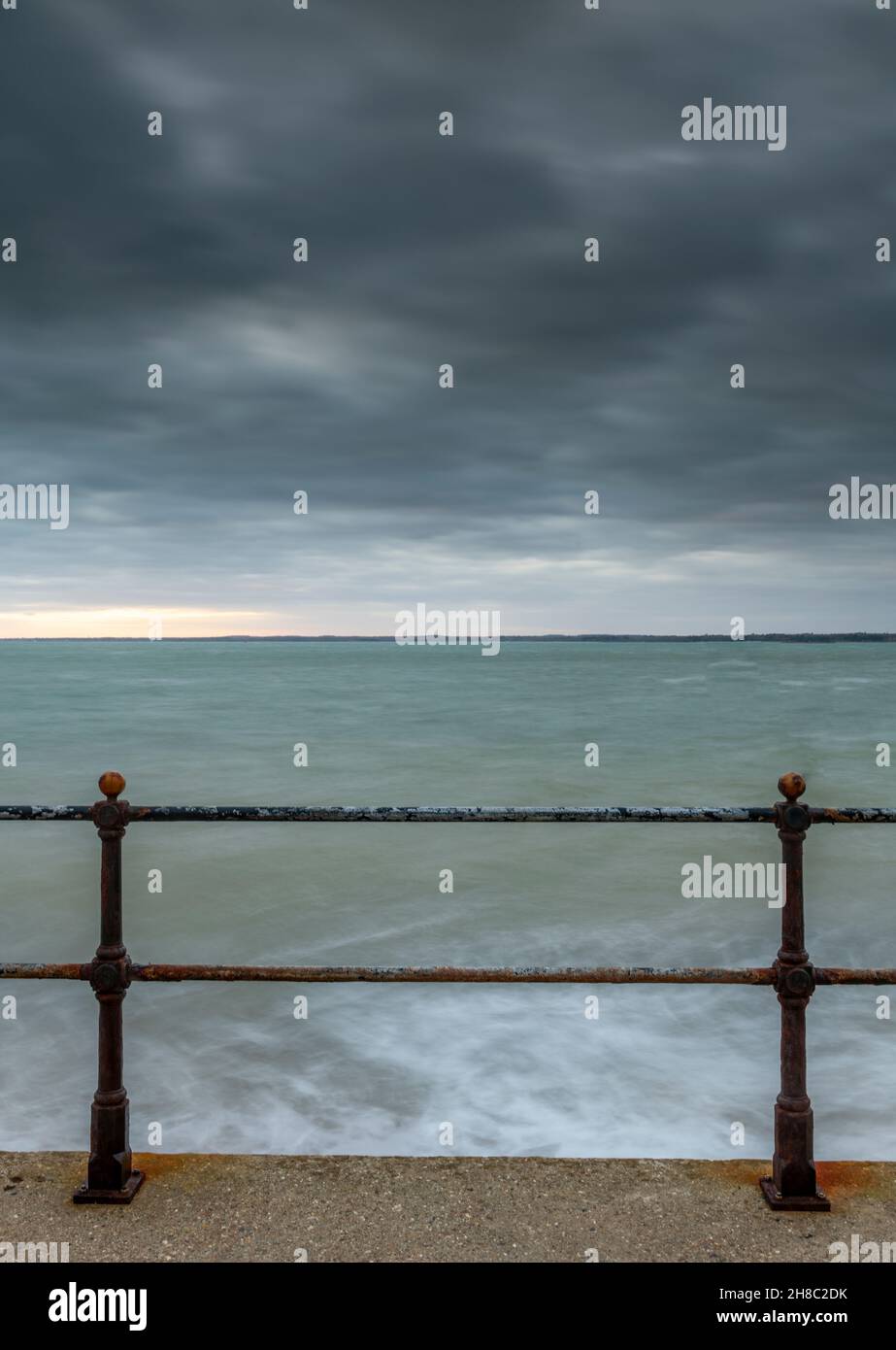 railings on the seashore with a dark brooding sky and flat sea ...