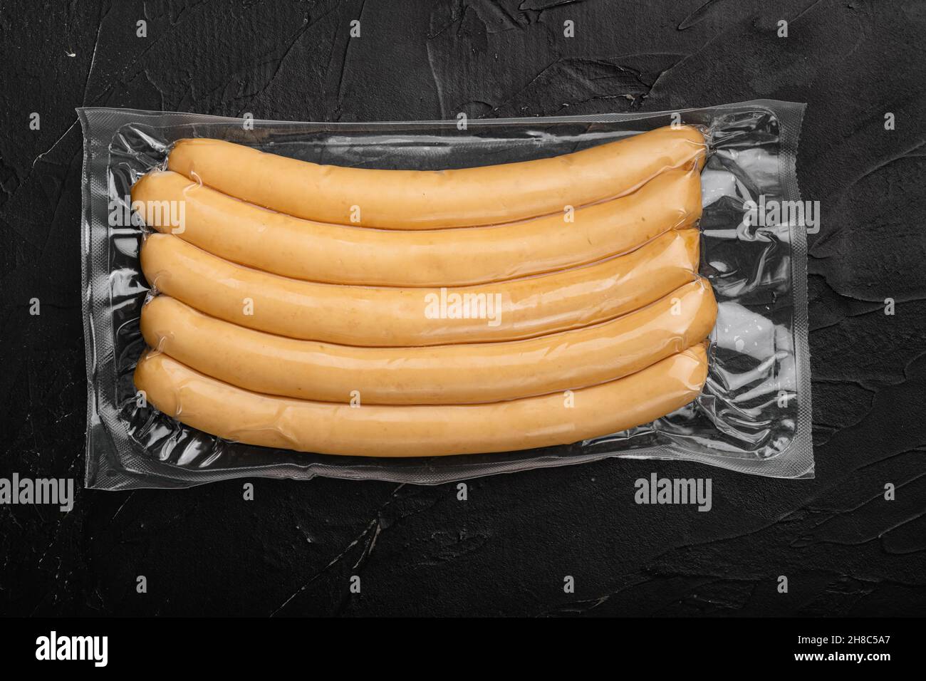 Raw chicken sausages in vacuum package set, on black dark stone table ...