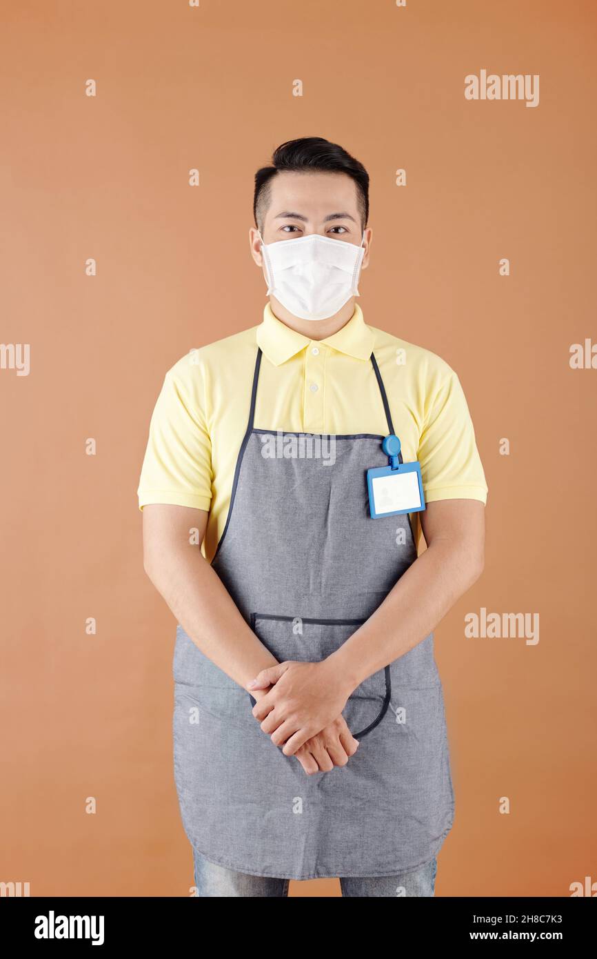 Waiter in medical mask and apron having badge on his chest Stock Photo ...