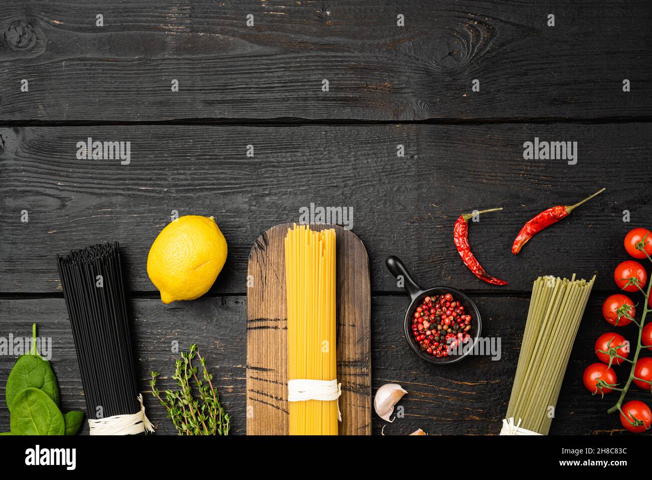 Multi colored spaghetti with ingredients set, on black wooden table ...