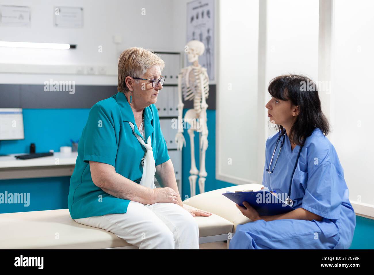 Medical assistant consulting aged woman with physical injury in office ...