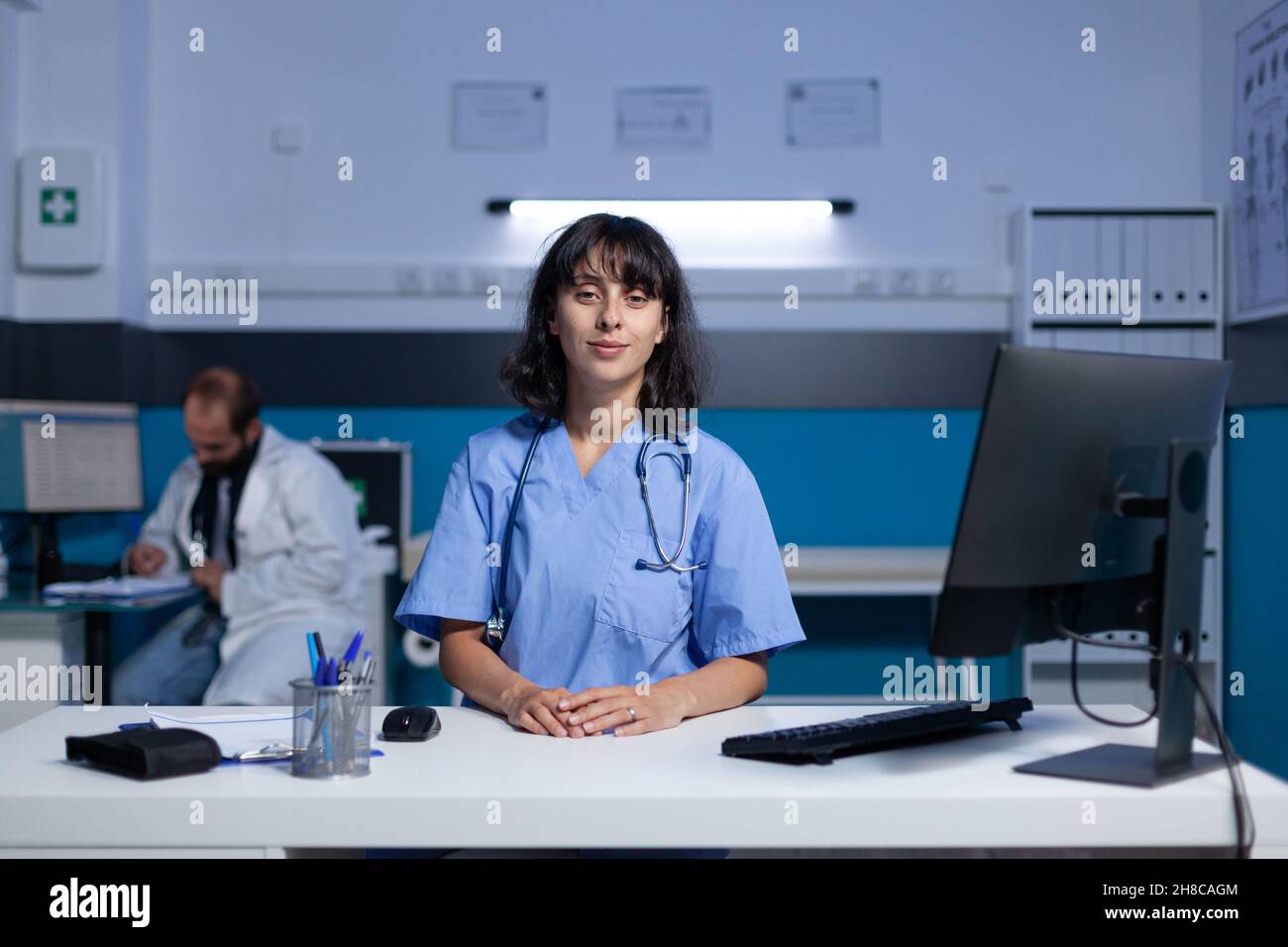 Portrait of medical assistant using computer at desk for work overtime ...