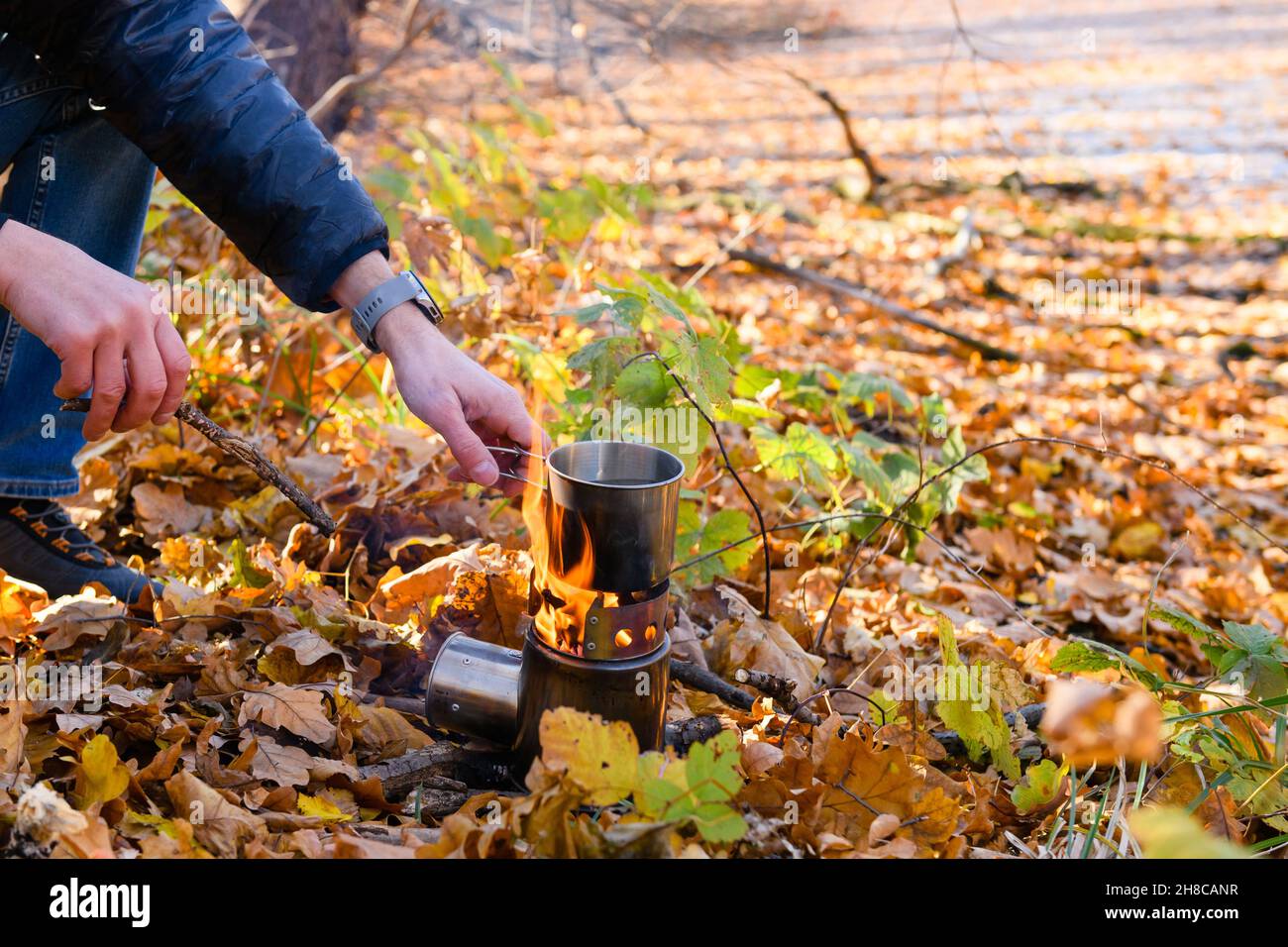 A tourist heats water in a metal mug on a fire in an autumn forest ...