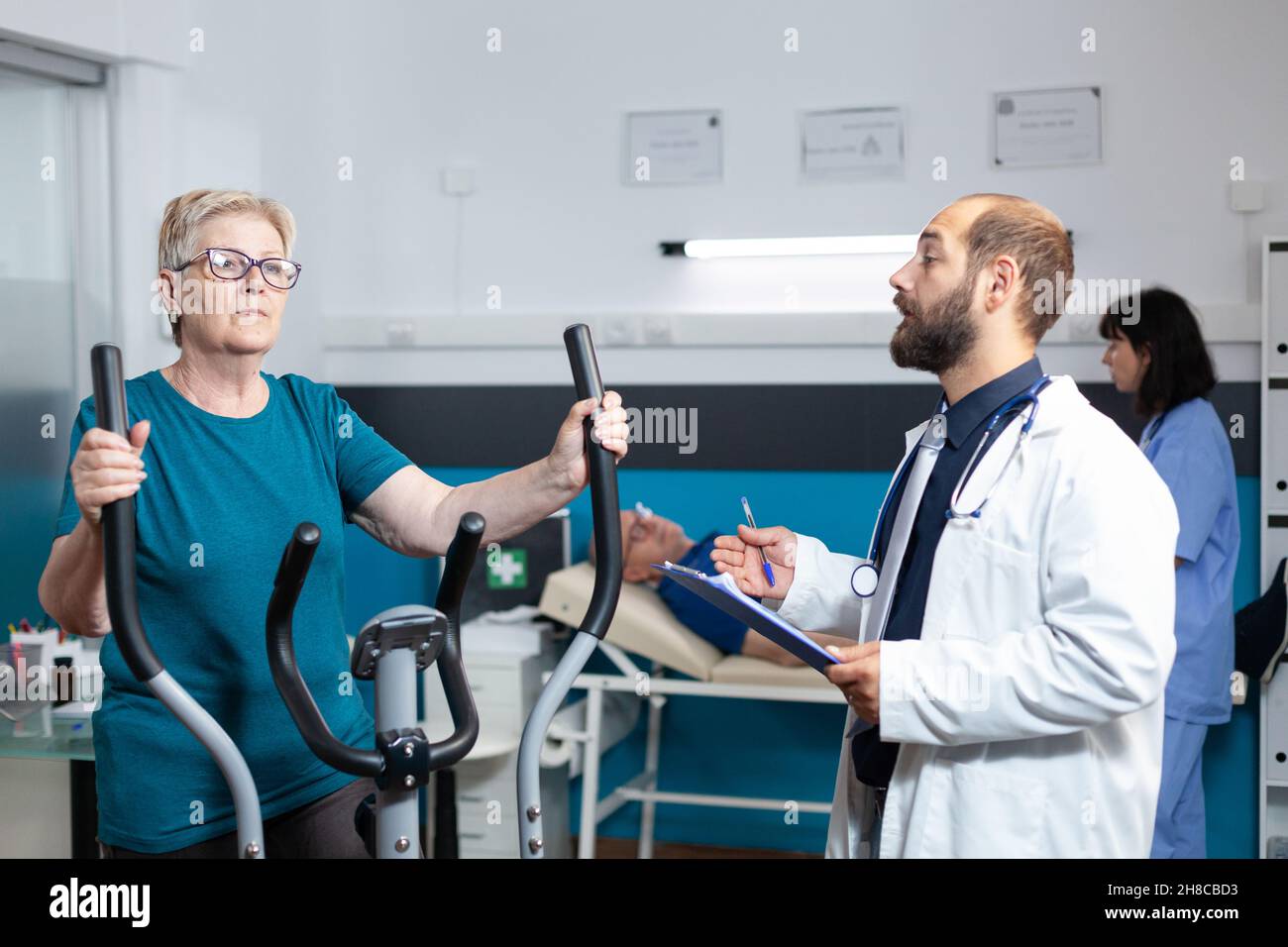 Old patient doing physical exercise with stationary bicycle while ...
