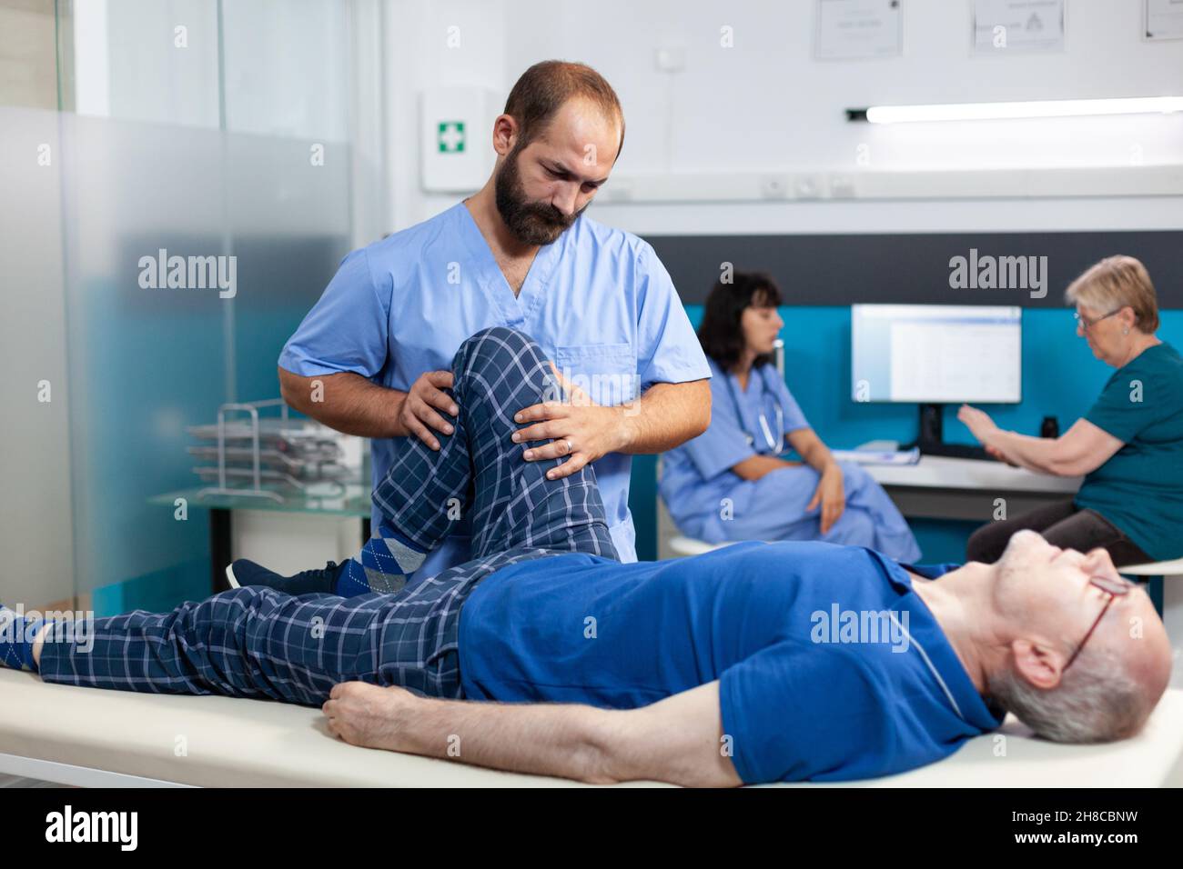 Physiotherapist helping aged man with leg injury to recover at ...