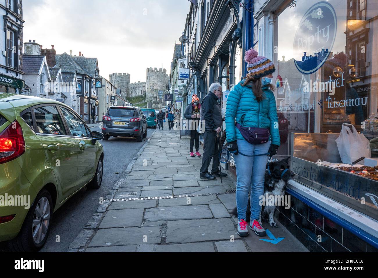 Female customers with pet dog queueing to shop in Popty of Conwy, Wales ...