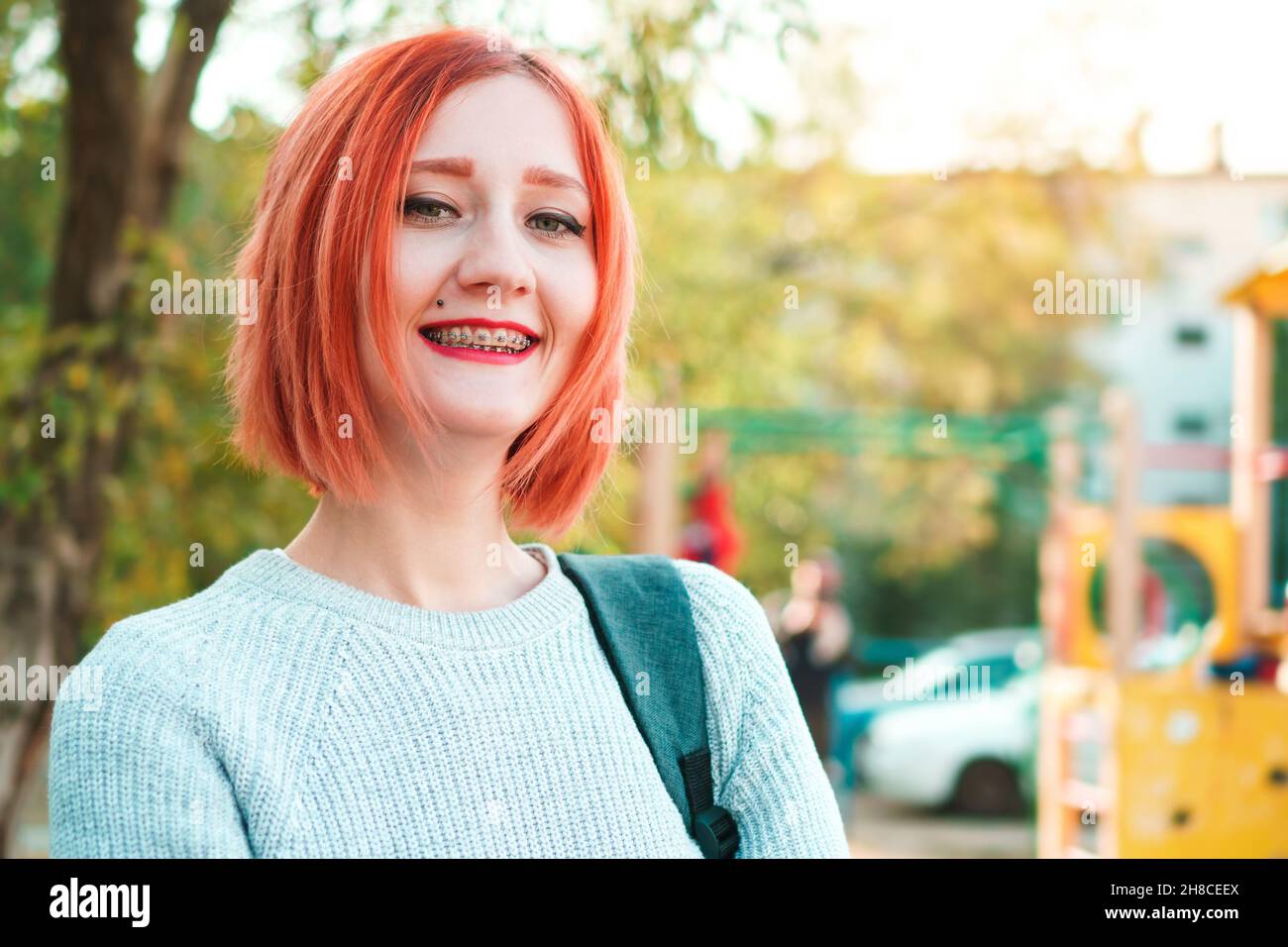 Ginger girl with orthodontic bracket and piercings smiles at background ...