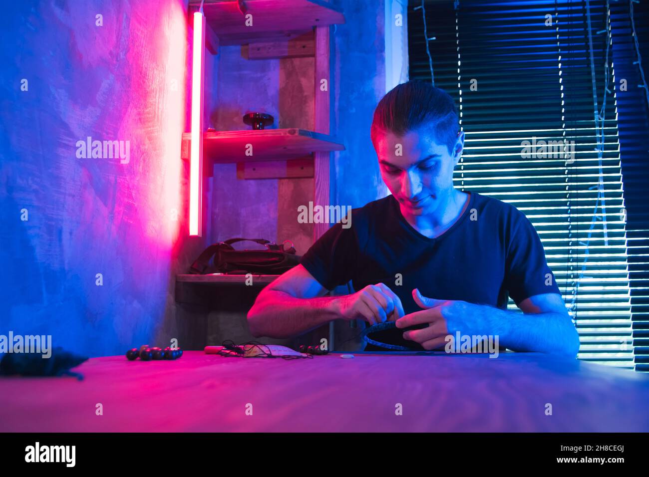 Man makes dreamcatcher in dark workshop illuminated by red and blue ...
