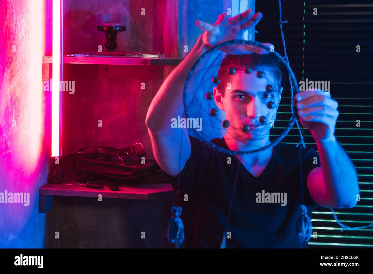 Craftsman shows dreamcatcher. Artisan in dark workshop illuminated by ...