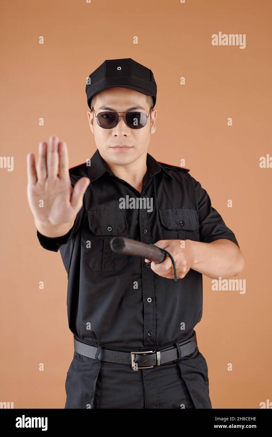 Portrait of serious police officer with baton in hands making stop ...
