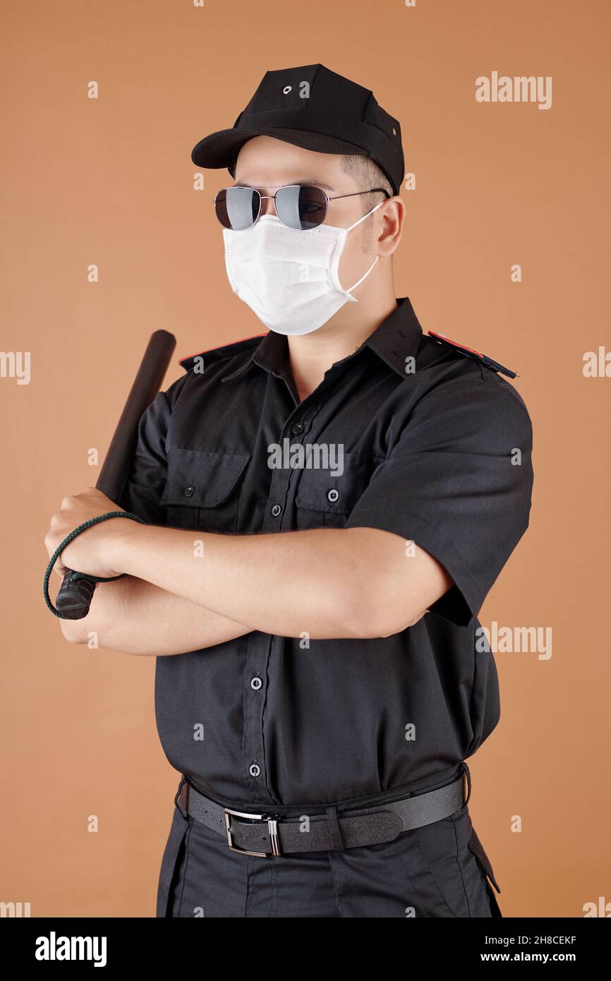 Confident police officer in sunglasses and protective mask standing ...