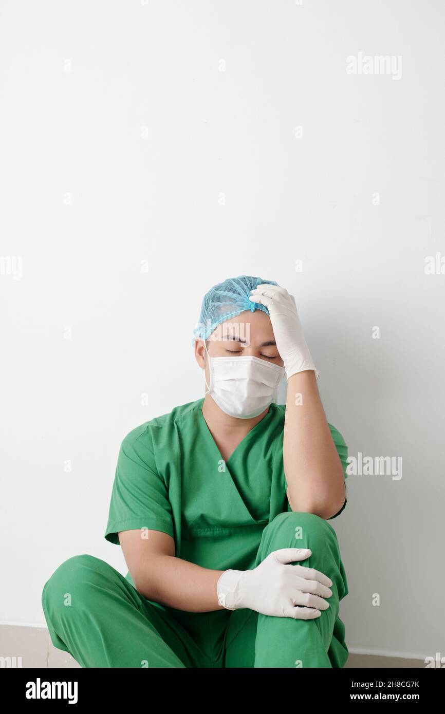Stressed exhausted surgeon sitting on the floor with eyes closed after ...