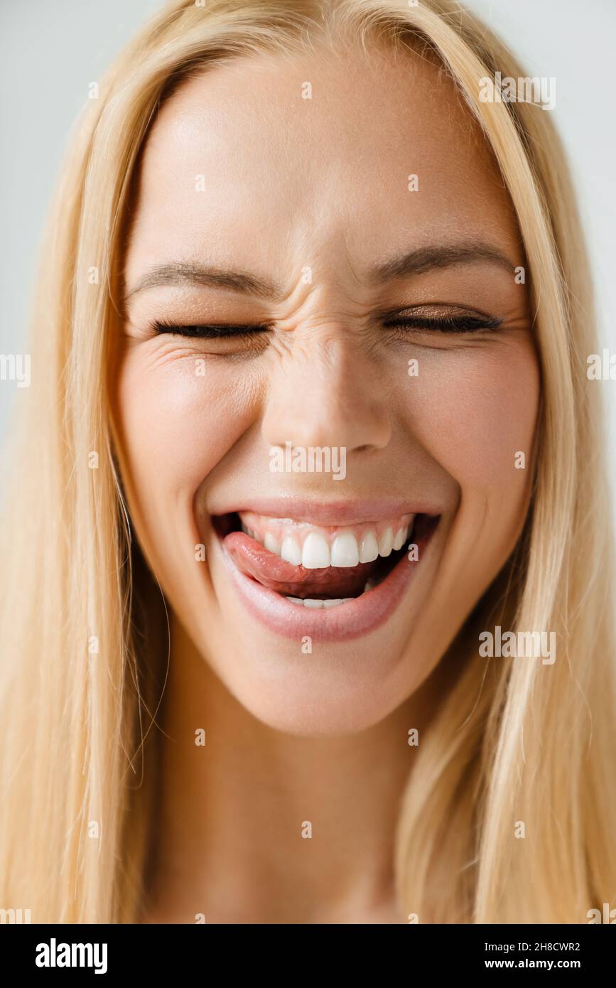Young blonde woman smiling while licking her teeth isolated over white ...