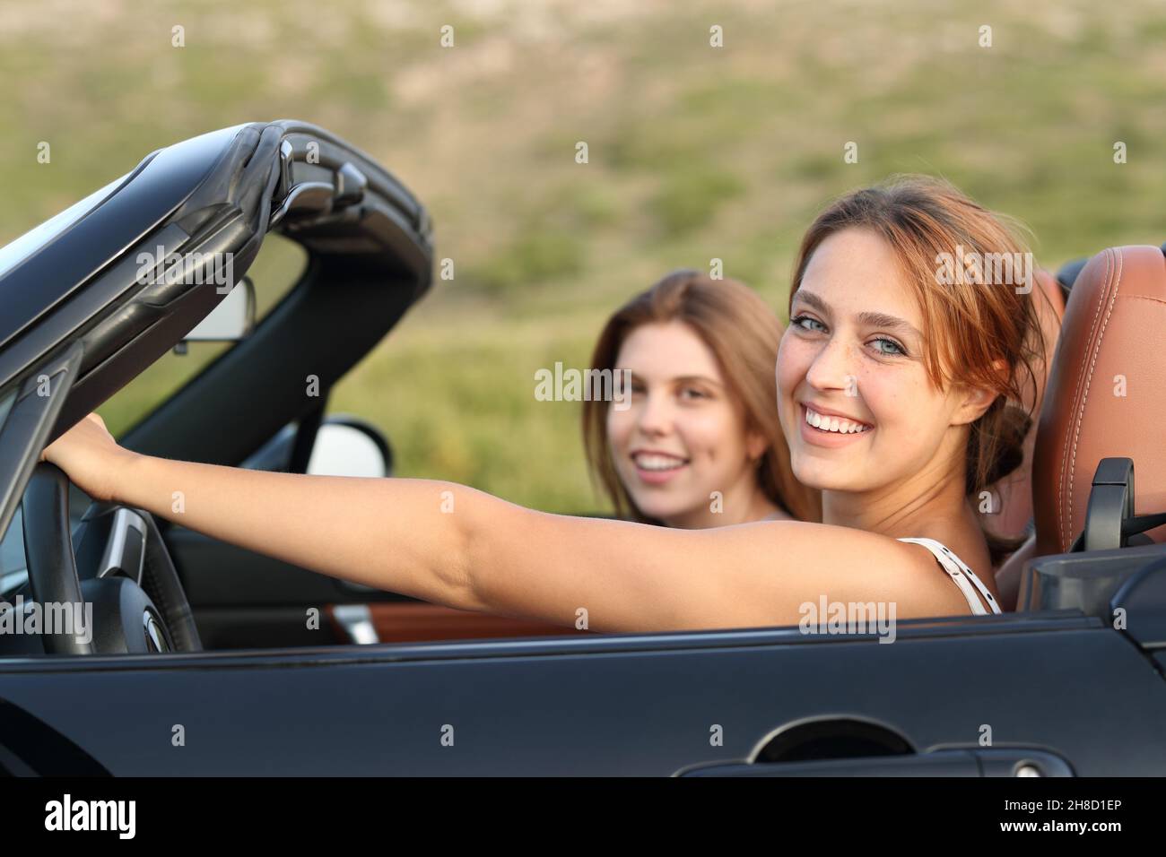 Two happy friends looking at you in a convertible car in the mountain ...