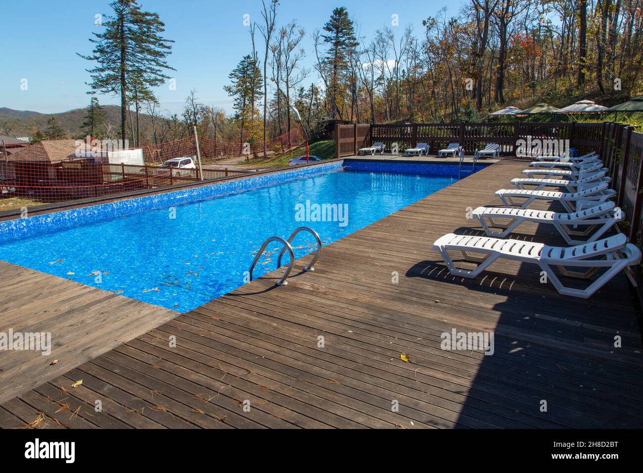 A large rectangular pool with blue water and dry leaves. White lounge ...