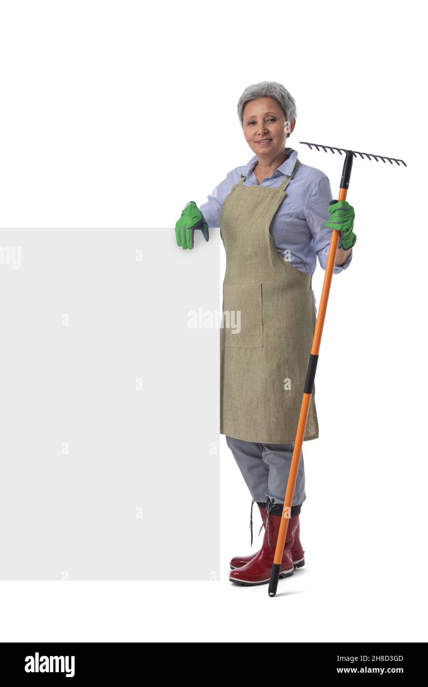 Mature asian woman gardener with rake standing behind blank banner with ...