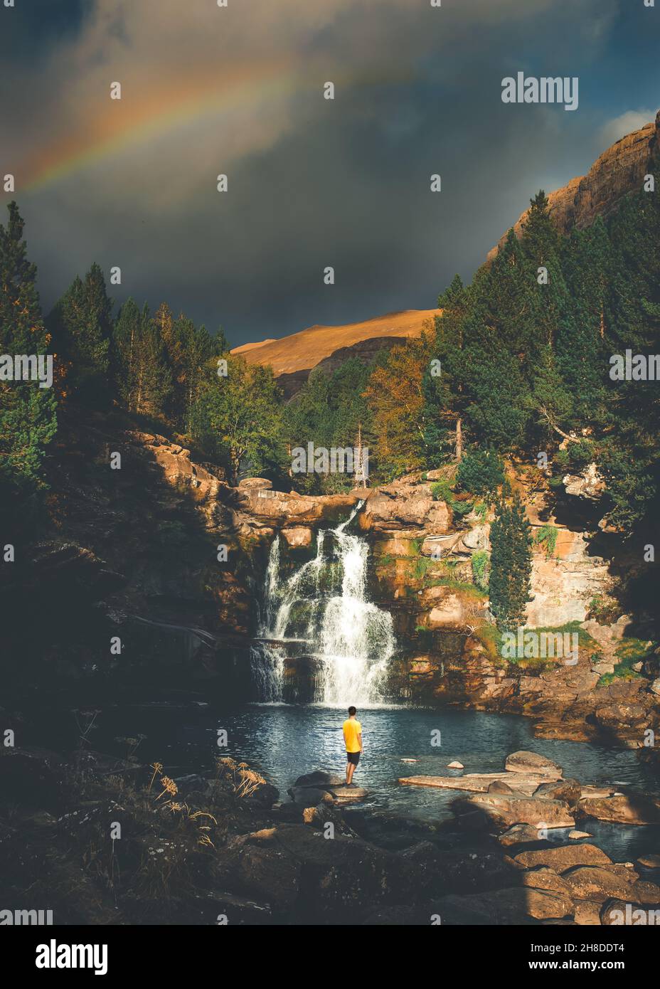 Glorious scenery of a rainbow in the sky above a waterfall flowing into ...