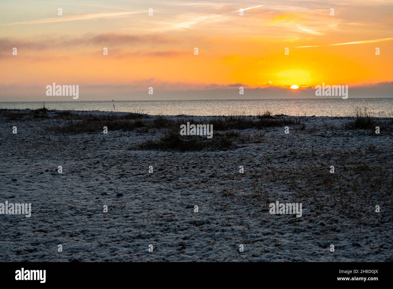 Sun rising over the sea with a thin layer of snow covering the shingle ...