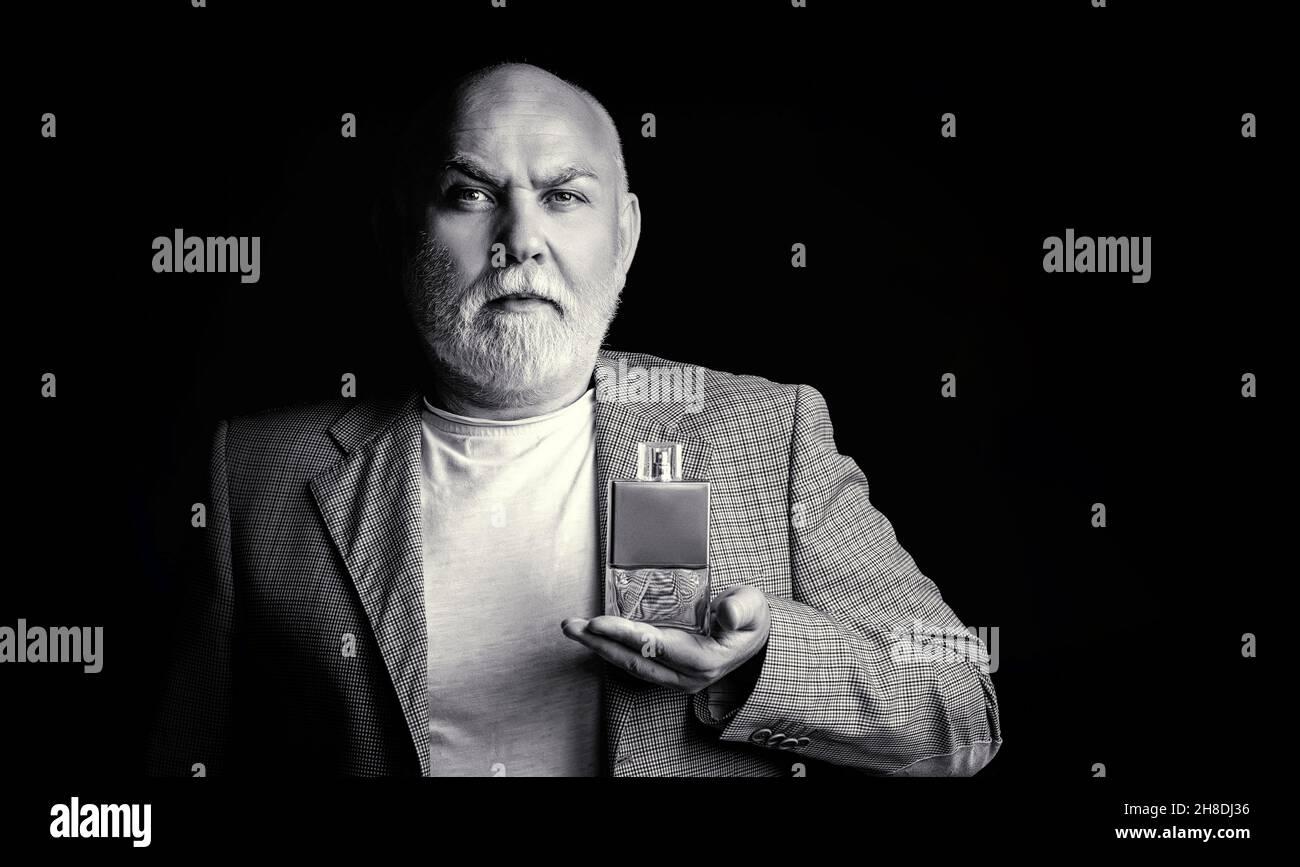 Masculine perfume, bearded old man in suit. Male holding up bottle of ...