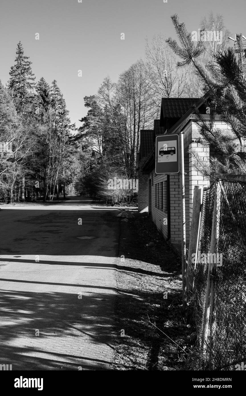 Vertical grayscale shot of the empty street with the bus stop sign ...