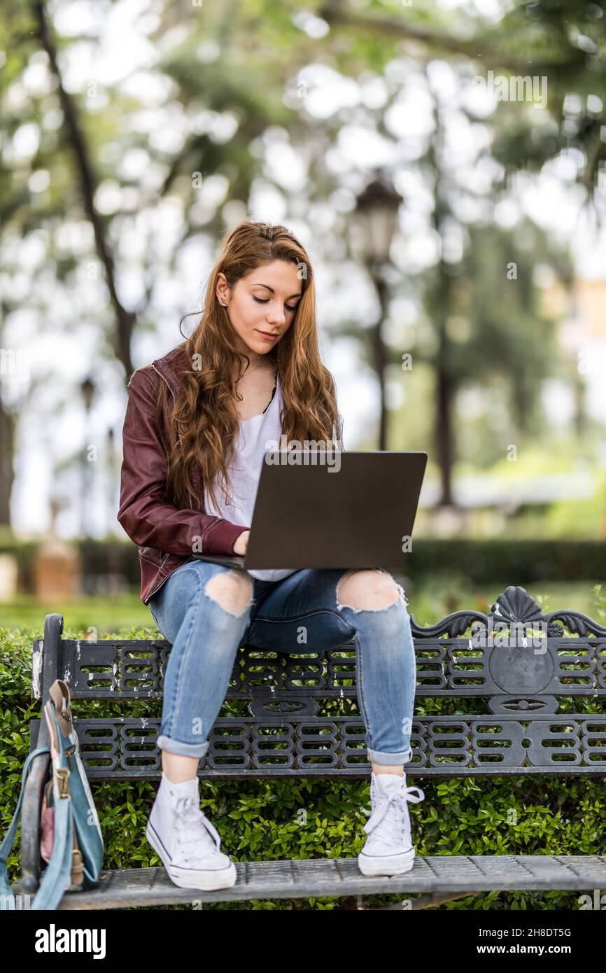 Young student working with a laptop sitting on a park bench Stock Photo ...