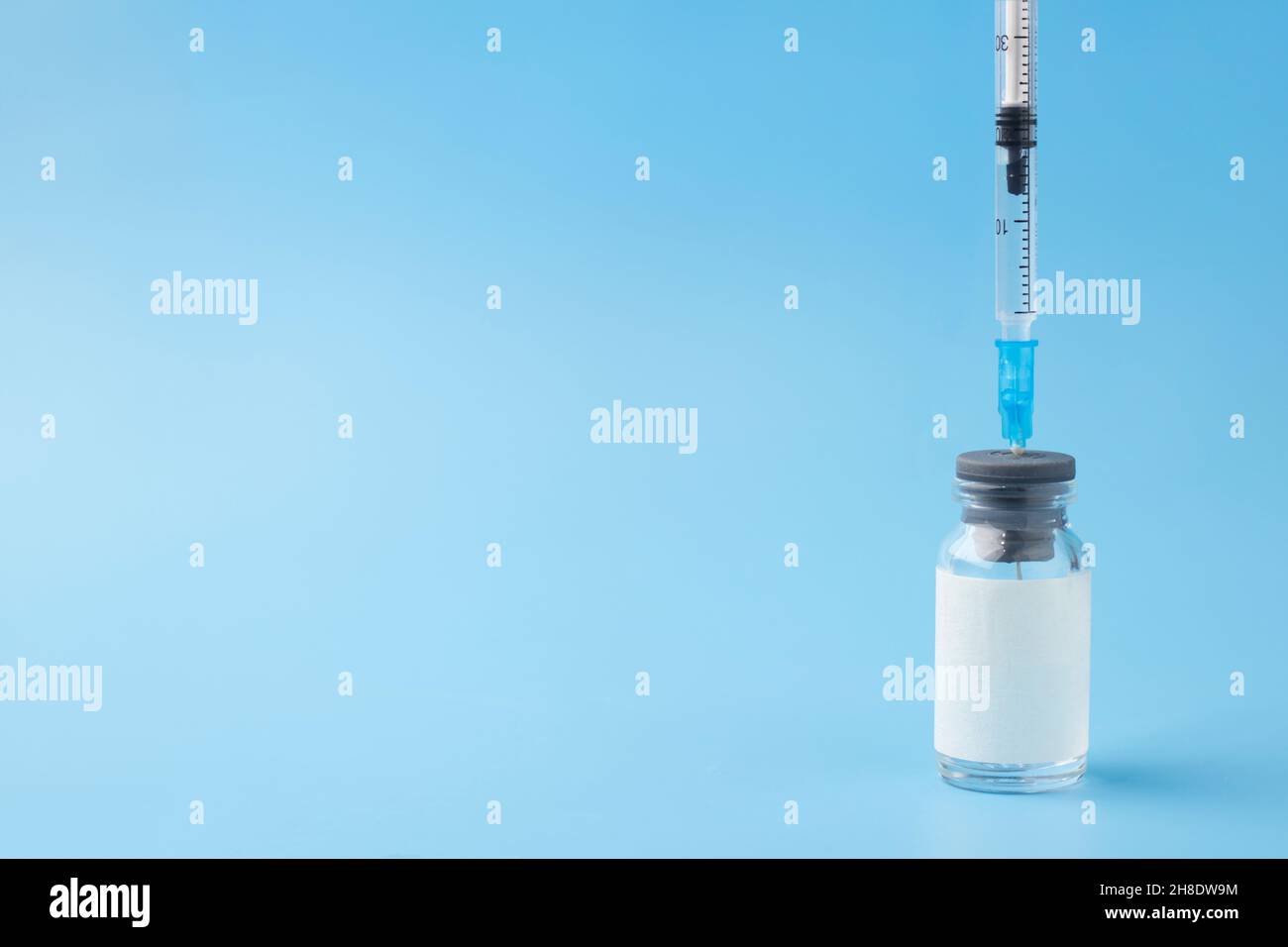 Medical glass bottle with copy space, with syringe inserted, on a blue ...