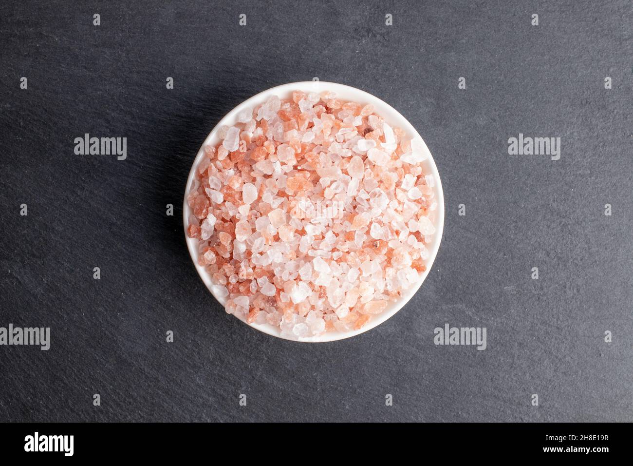 Pink rock salt in a ceramic salt shaker, close-up, on a slate serving ...