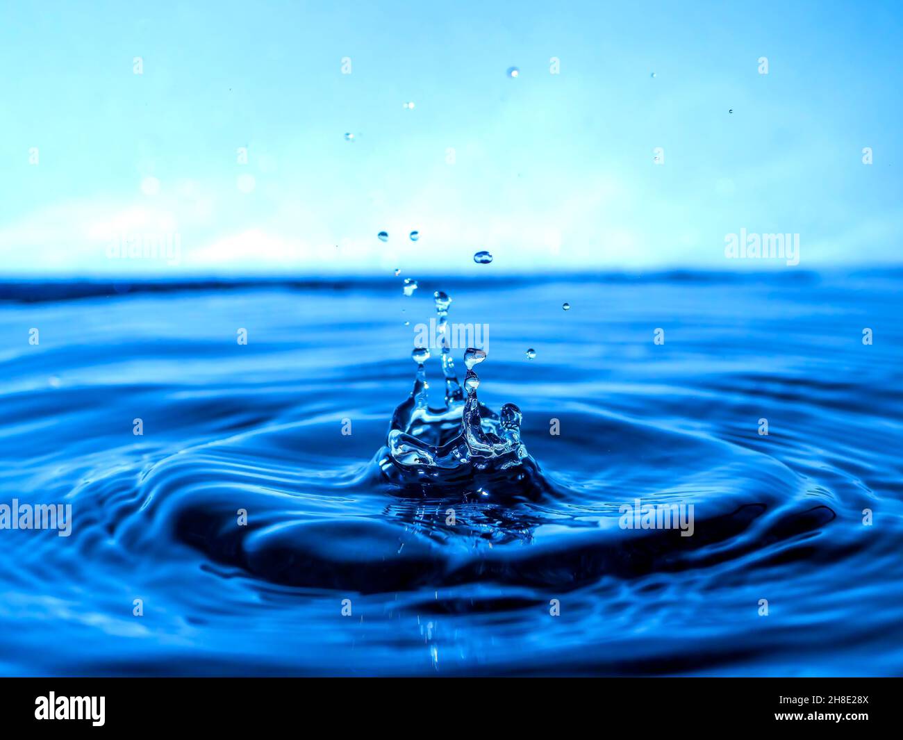 A blue drop drips into the water and creates splashes of various shapes ...