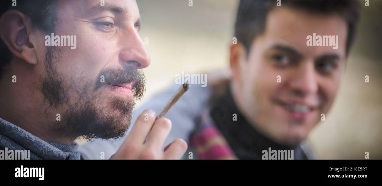 Two relaxed and smiling happy young friends smoking cannabis marijuana ...