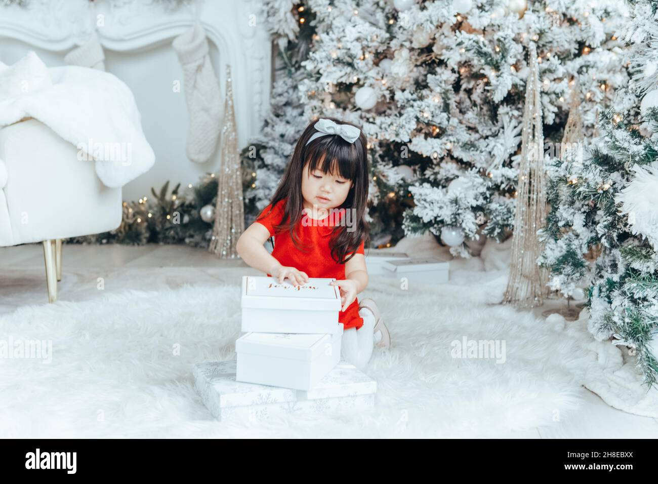 Asian toddler girl in red dress opening gift boxes with presents under ...