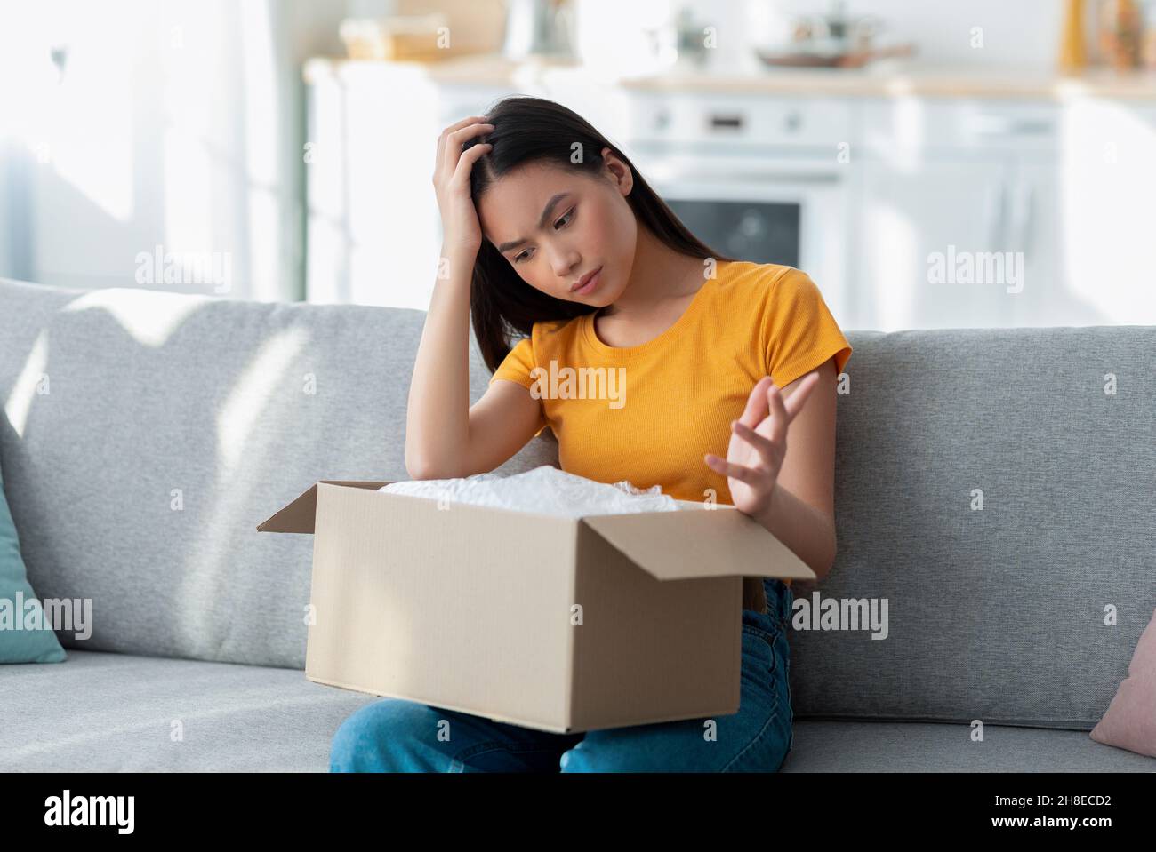 Damaged package. Disappointed asian lady unboxing her delivery, looking ...