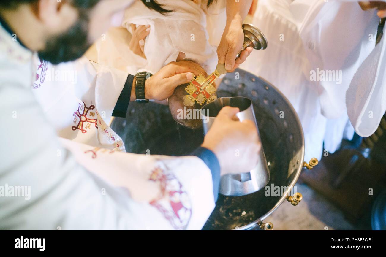 Priest washes the baby head from a jug during baptism over a basin ...