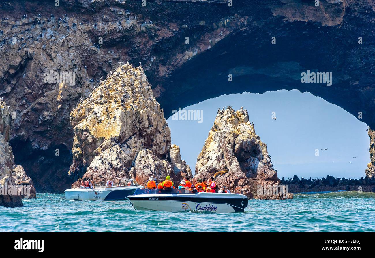 Tourists, in boats, watching birds flying under the natural rock arch ...