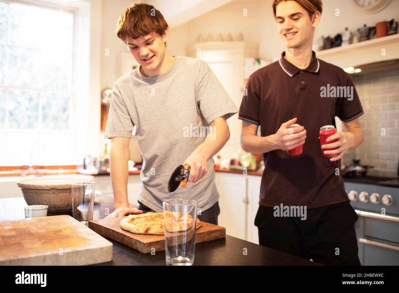 Teenage boys slicing pizza in kitchen Stock Photo - Alamy